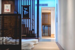 Um corredor com uma cama, um painel de madeira e uma porta que dá para outro quarto.