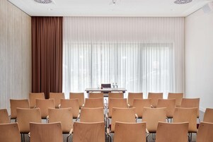 Sala de conferência com fileiras de cadeiras voltadas para uma mesa com projetor.