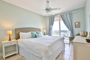 Quarto com cama, mesas de cabeceira, ventoinha no teto, janela com cortinas e vista para o exterior.