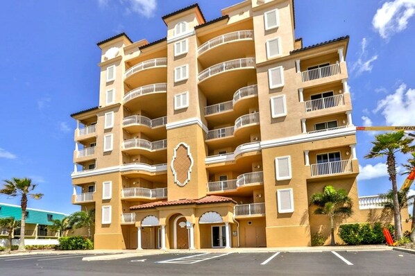 Um hotel com vários andares, varandas, entrada central e estacionamento.