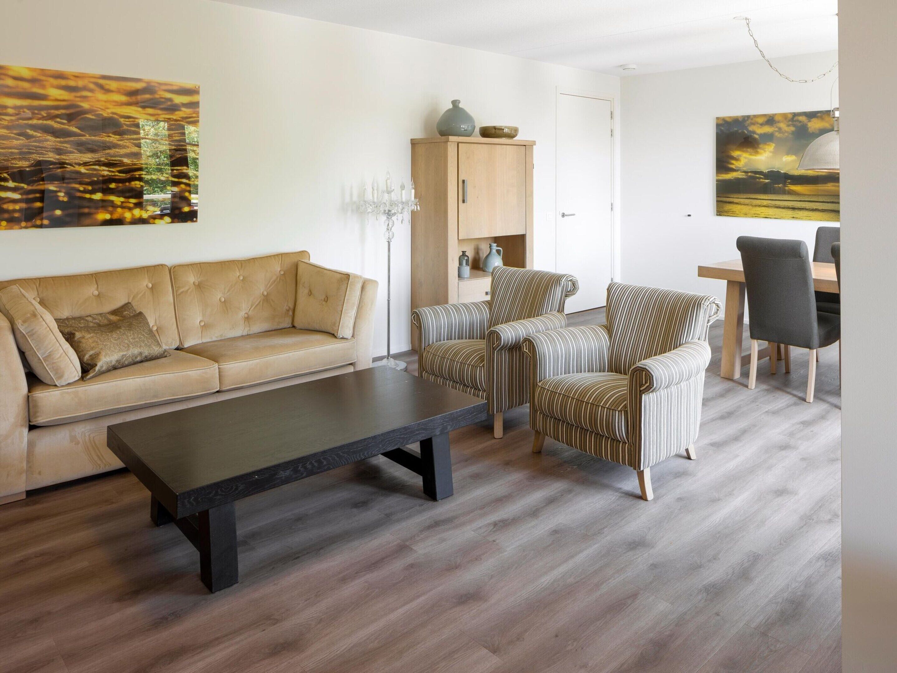 Uma sala de estar moderna com um sofá, poltronas listradas, uma mesa de centro e uma área de jantar com cadeiras.