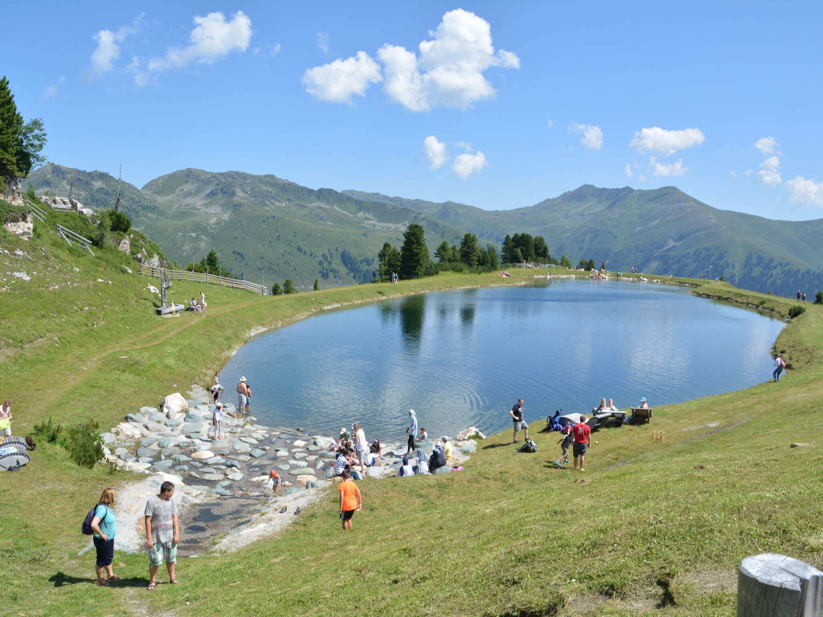 Um lago rodeado por montanhas, com pessoas desfrutando do ambiente ao ar livre.