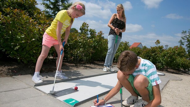 Três pessoas jogando croquet num dia ensolarado.