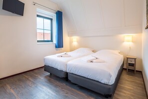 Quarto com cama, duas mesas de cabeceira, janela com cortinas e televisão fixada na parede.
