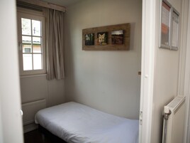 Quarto pequeno com uma cama de solteiro, janela, radiador e três quadros na parede.