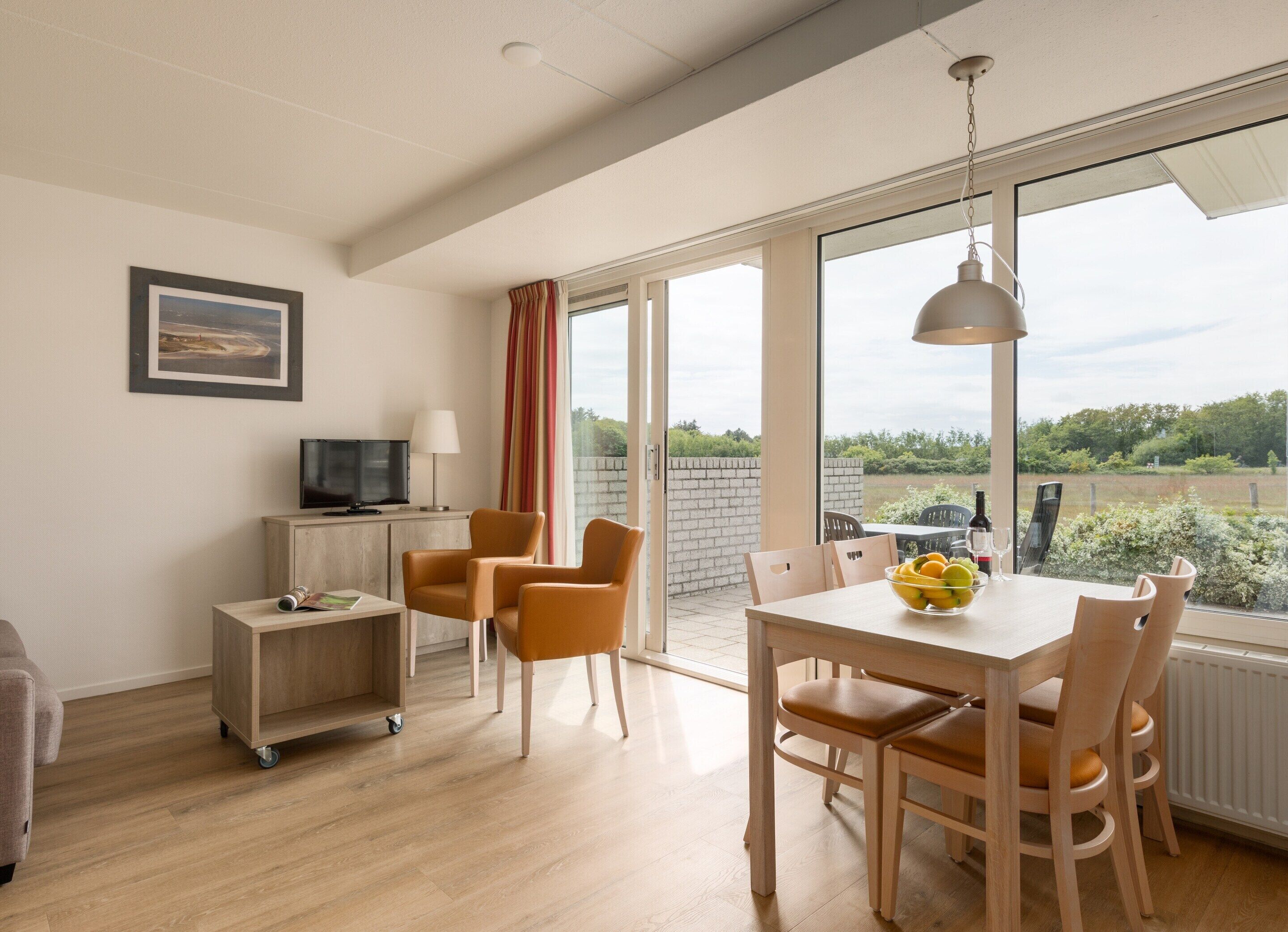 Quarto moderno com área de refeições, TV e vista para o exterior.