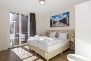 Quarto de hotel com uma cama, um quadro, uma mesa de cabeceira e vista através de uma porta de correr.
