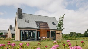 Uma casa moderna com telhado inclinado, grandes janelas e um jardim bem cuidado com flores cor-de-rosa.