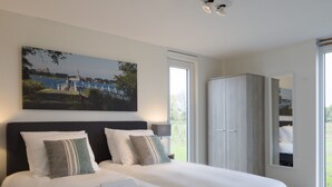 Um quarto moderno com uma cama grande, um quadro de uma paisagem e um guarda-roupa.