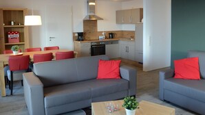 Uma sala de estar moderna com um sofá cinzento, almofadas vermelhas, uma mesa de centro de madeira e um espaço de jantar com cadeiras vermelhas.