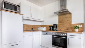 Cozinha moderna com armários brancos, micro-ondas de aço inoxidável, torradeira, cafeteira e forno.