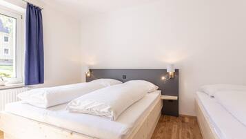 Quarto de hotel com cama de casal, mesa de cabeceira, cortinas na janela e vista para um prédio.