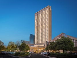 Um edifício de hotel alto com design moderno, apresentando uma entrada ampla e uma área de estacionamento com vários carros.