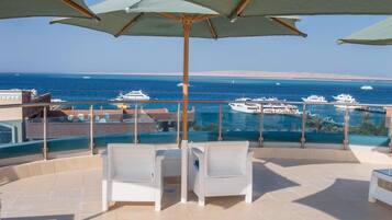 Um terraço com mobiliário de vime branco, uma mesa de vidro com bebidas e vista para o mar e iates.