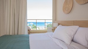 Quarto de hotel com uma cama, vista para o mar e varanda com cadeira de vime.