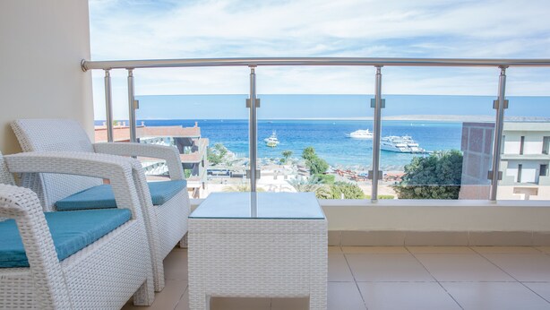 Varanda com mobiliário de vime branco e mesa de vidro, com vista para a área costeira com barcos e edifícios.