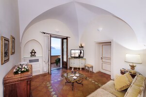 Uma sala de estar ampla com uma mesa de centro de vidro, um sofá e vista para o exterior através de uma porta aberta.