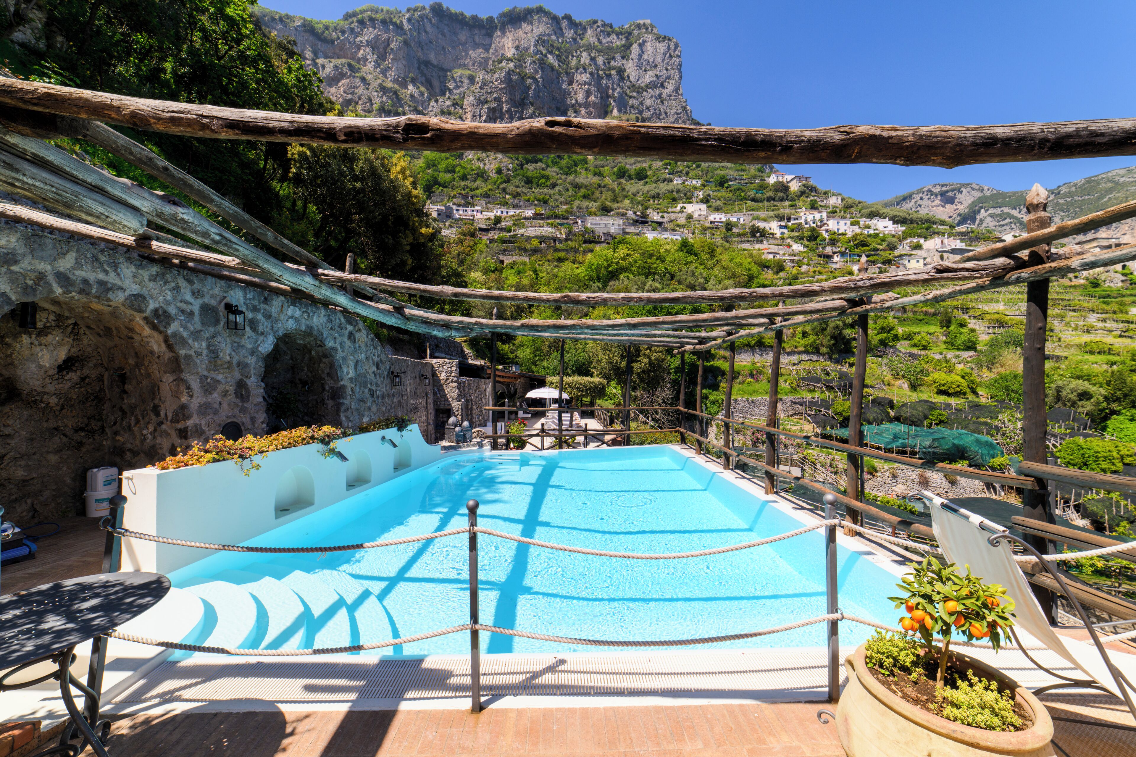 Área de piscina com vista para uma paisagem montanhosa, paredes de pedra e vigas de madeira.