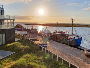 Um cais à beira-mar com barcos, um edifício com fachada de vidro e uma vista desobstruída do pôr do sol sobre a água.