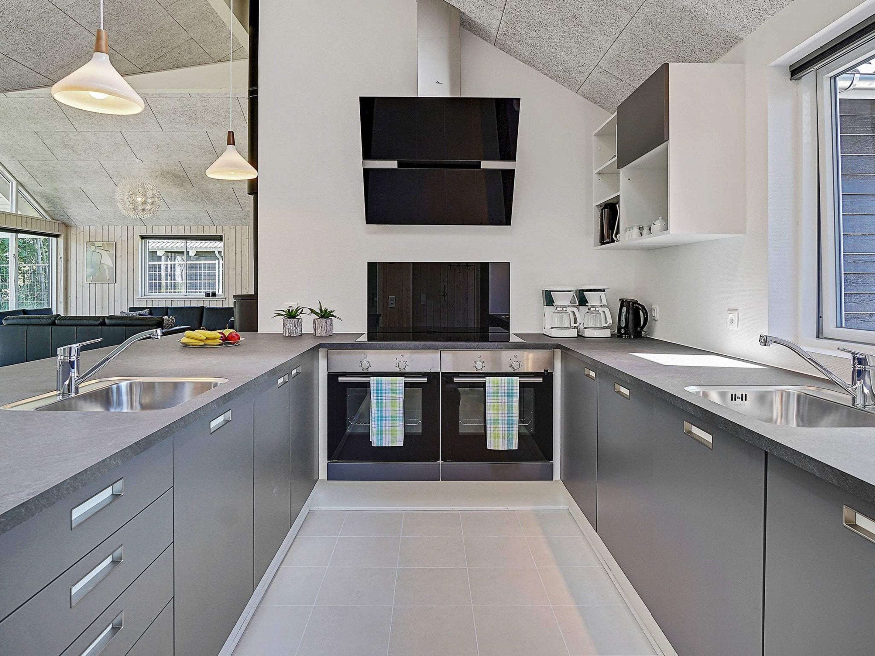 Cozinha moderna com ilha central, eletrodomésticos embutidos e iluminação pendente.