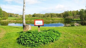 Cenário tranquilo à beira do lago, com uma placa de sinalização, vegetação exuberante e céu claro.