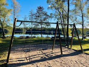 Um balanço em um parque com mesas de piquenique e um lago ao fundo.