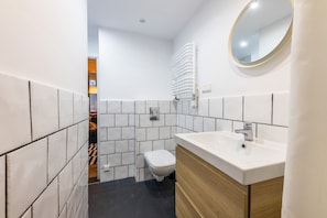 Casa de banho moderna com azulejos brancos, sanita branca, lavatório com espelho e um porta-toalhas.