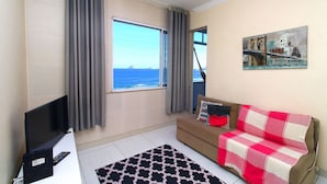 Um quarto com uma janela grande, um sofá, uma televisão e um quadro.