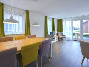 Uma sala de estar moderna com uma mesa de jantar de madeira, assentos confortáveis, uma TV e uma porta de vidro deslizante que dá para uma área externa.