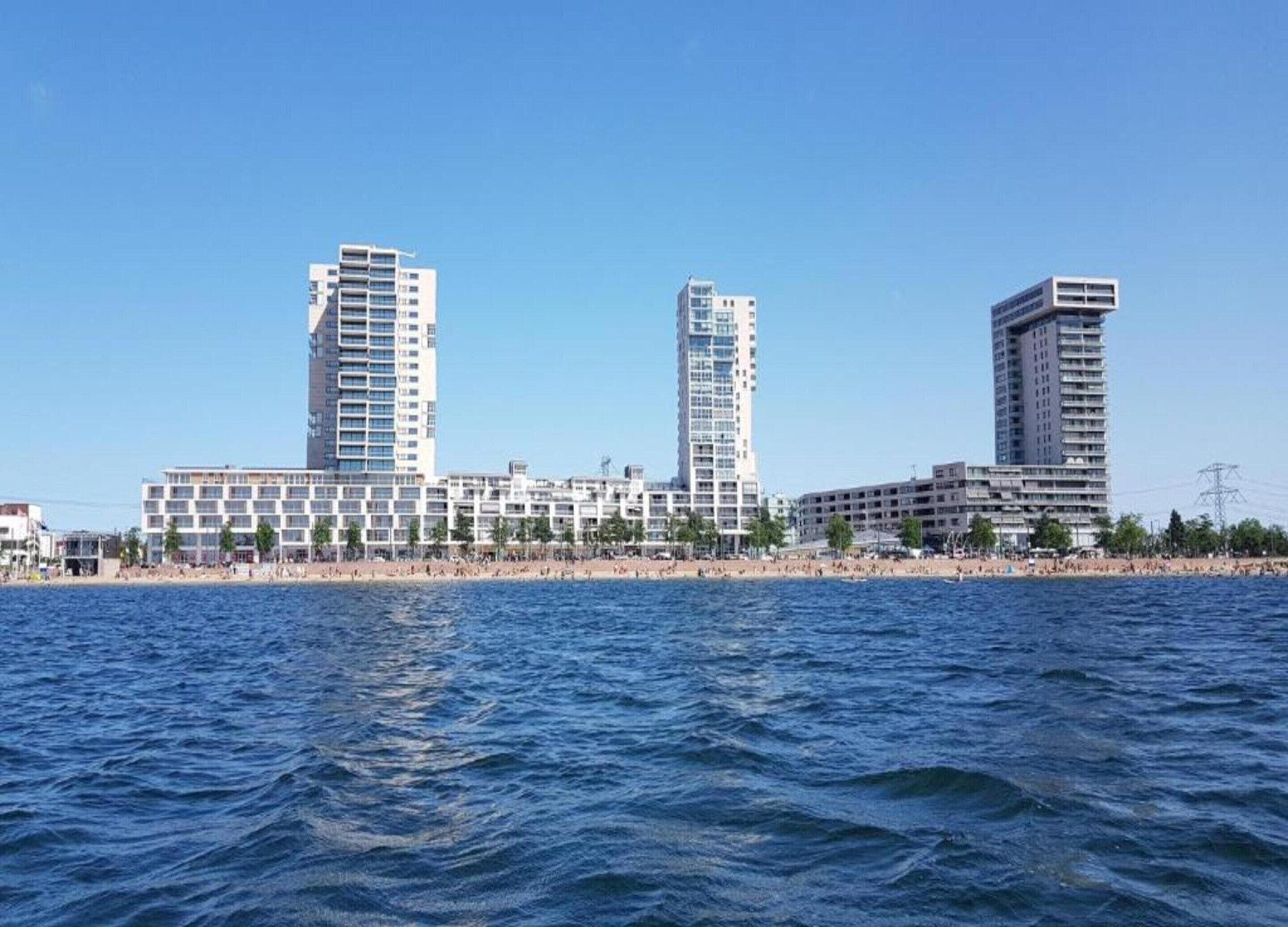 Paisagem costeira urbana com edifícios modernos altos, uma praia e vista para o mar.