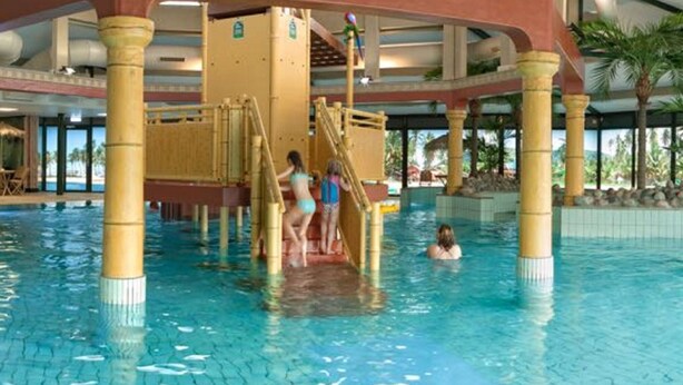 Piscina interna com um toboágua central, cercada por pilares e um deck coberto.