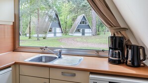 Uma cozinha compacta com pia, cafeteira e vista para duas casas na árvore.