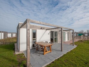 Um pátio moderno ao ar livre com mesa e cadeiras de madeira, envolto por uma pérgola de madeira.