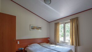 Quarto com duas camas, um guarda-roupa de madeira, um quadro emoldurado na parede, uma janela com cortinas e um radiador.