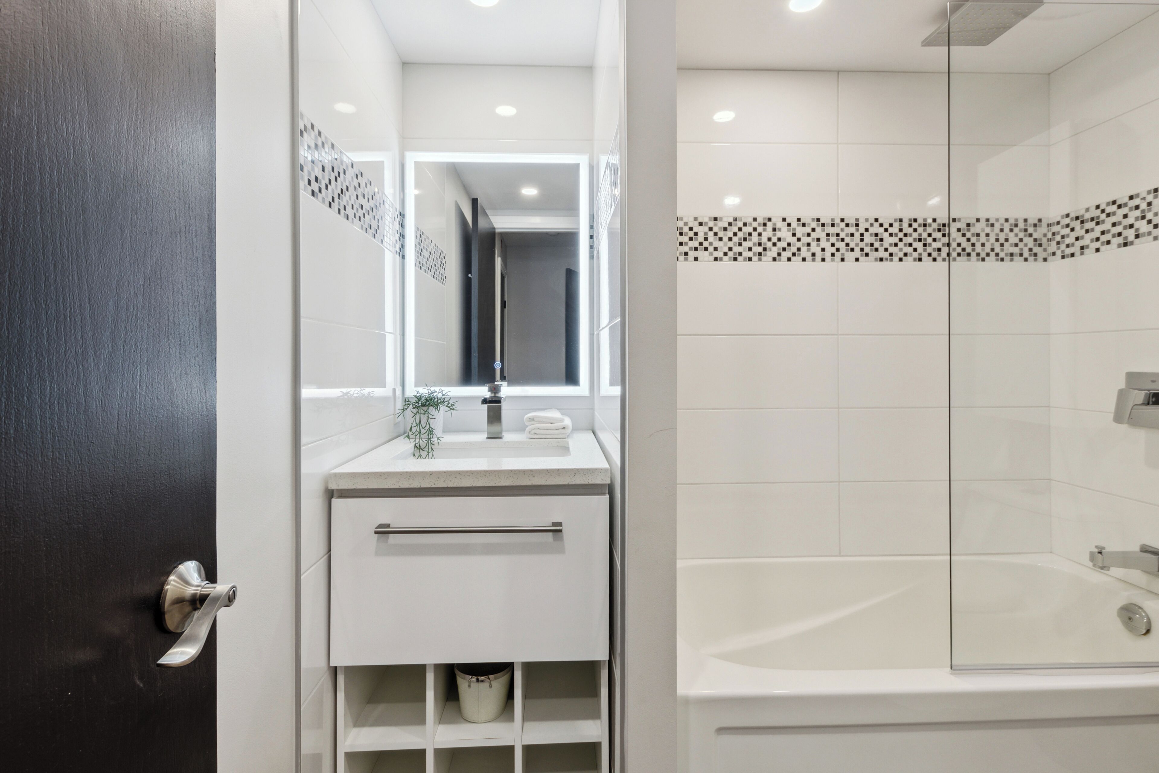 Casa de banho moderna com divisória de chuveiro em vidro, azulejos brancos e lavatório embutido com espelho.