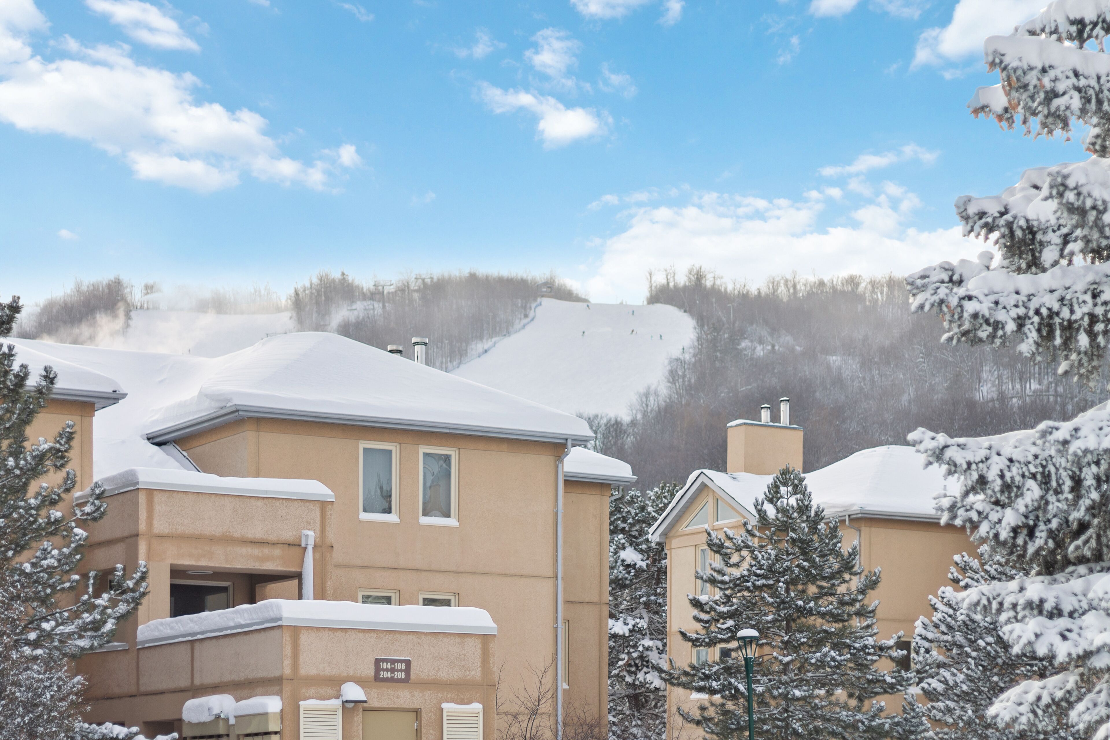 Um edifício residencial com telhado coberto de neve e vista para uma paisagem nevada ao fundo.
