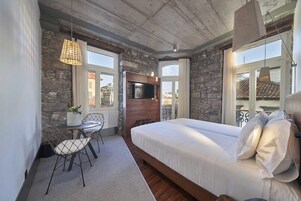 Quarto com cama grande, paredes de pedra, TV e varanda com vista.