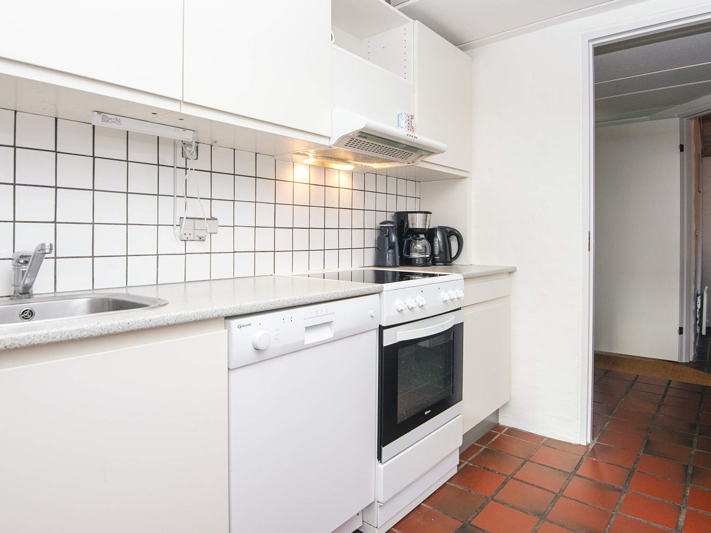 Cozinha compacta com armários brancos, pia de aço inoxidável, fogão a gás e forno embutido.