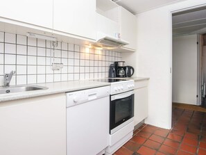 Cozinha compacta com armários brancos, pia de aço inoxidável, fogão a gás e forno embutido.