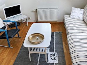 Uma sala de estar com uma mesa branca, uma cadeira preta, um sofá listrado, um radiador e uma televisão.