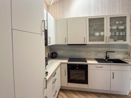 Uma cozinha moderna com armários brancos, bancada preta, forno embutido e máquina de lavar louça.
