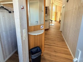 Um corredor estreito com paredes de madeira, um espelho, uma pia pequena e uma lixeira.