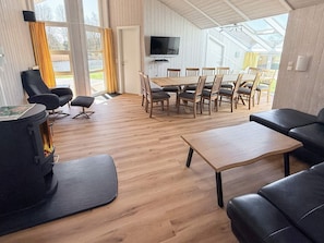Uma sala de estar acolhedora com lareira, mesa de jantar com cadeiras e uma TV fixada na parede.