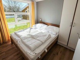 Quarto com cama, cabeceira de madeira e janela com cortinas.