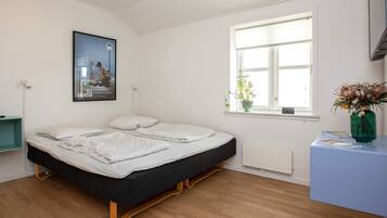Quarto com cama, janela com vista, mesa de cabeceira e um pôster na parede.