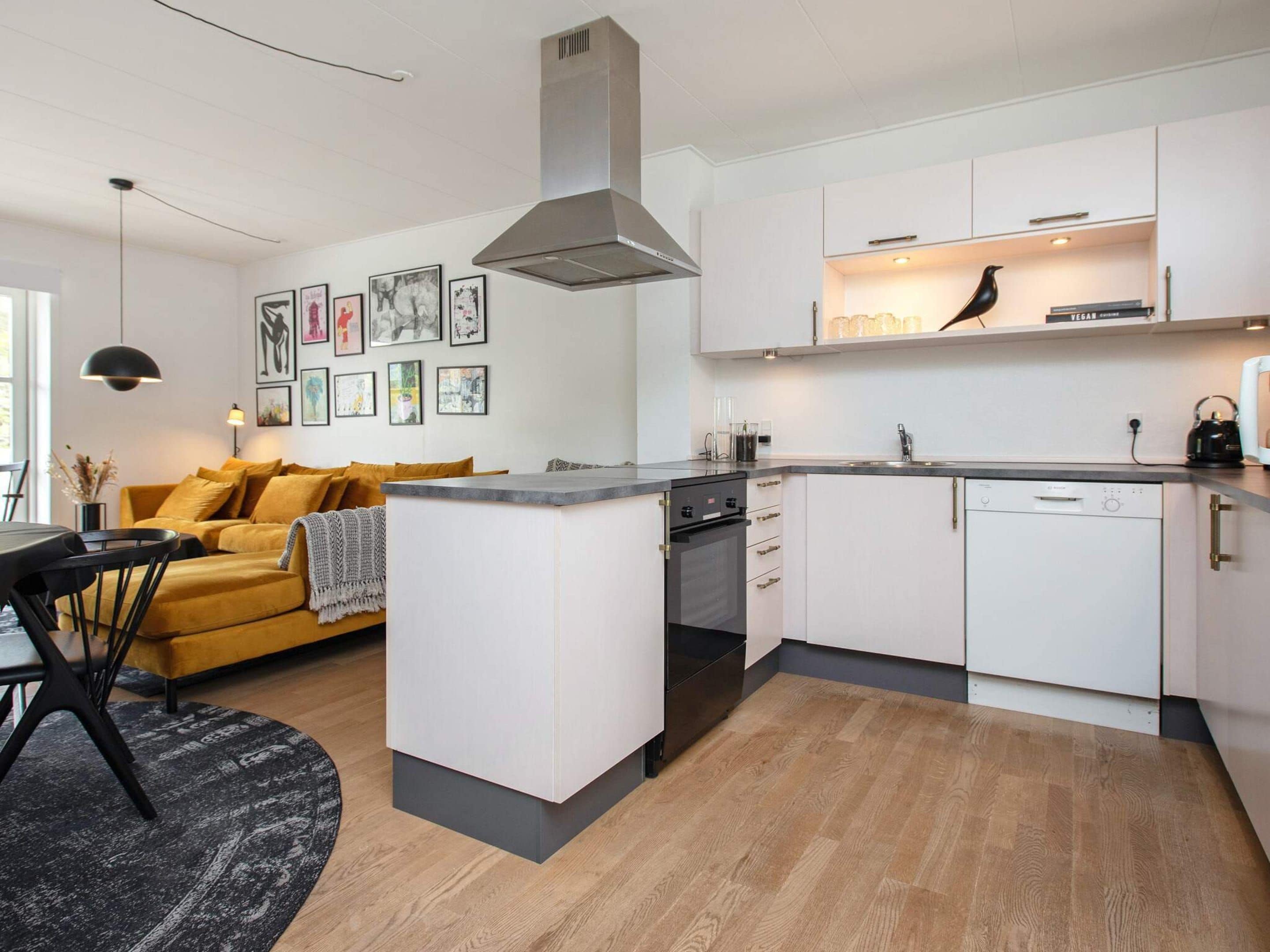 Cozinha moderna com armários brancos, uma ilha central e um espaço de refeições com sofá amarelo.