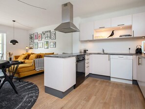 Cozinha moderna com armários brancos, uma ilha central e um espaço de refeições com sofá amarelo.
