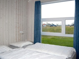 Quarto com uma janela grande, cama com roupa de cama branca e parede de madeira.