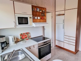 Cozinha compacta equipada com micro-ondas, forno e frigorífico. Há um suporte de madeira para temperos sobre o micro-ondas e uma máquina de café na bancada.