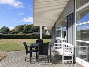 Um pátio externo com mesa e cadeiras, um banco branco e vista para uma área residencial.